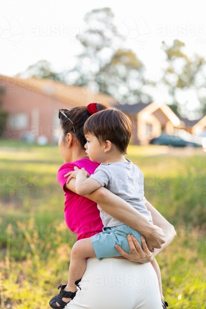Image of Mum giving toddler piggyback ride in suburban green strip park ...