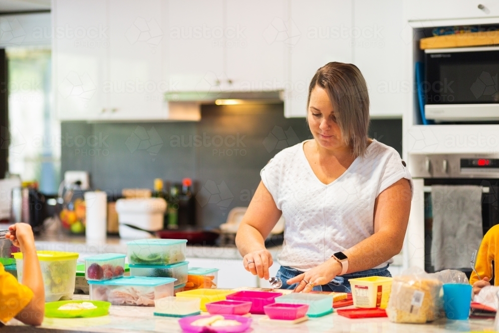 Image of Mum in kitchen making school lunches while kids eat breakfast ...