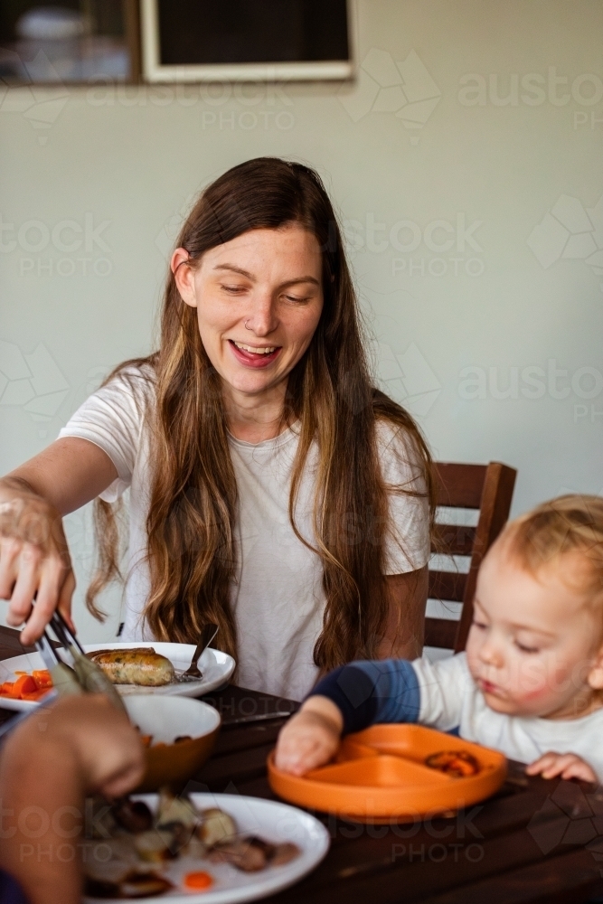 Image of mum serving up her dinner wile toddler eats at family BBQ in backyard at home ...
