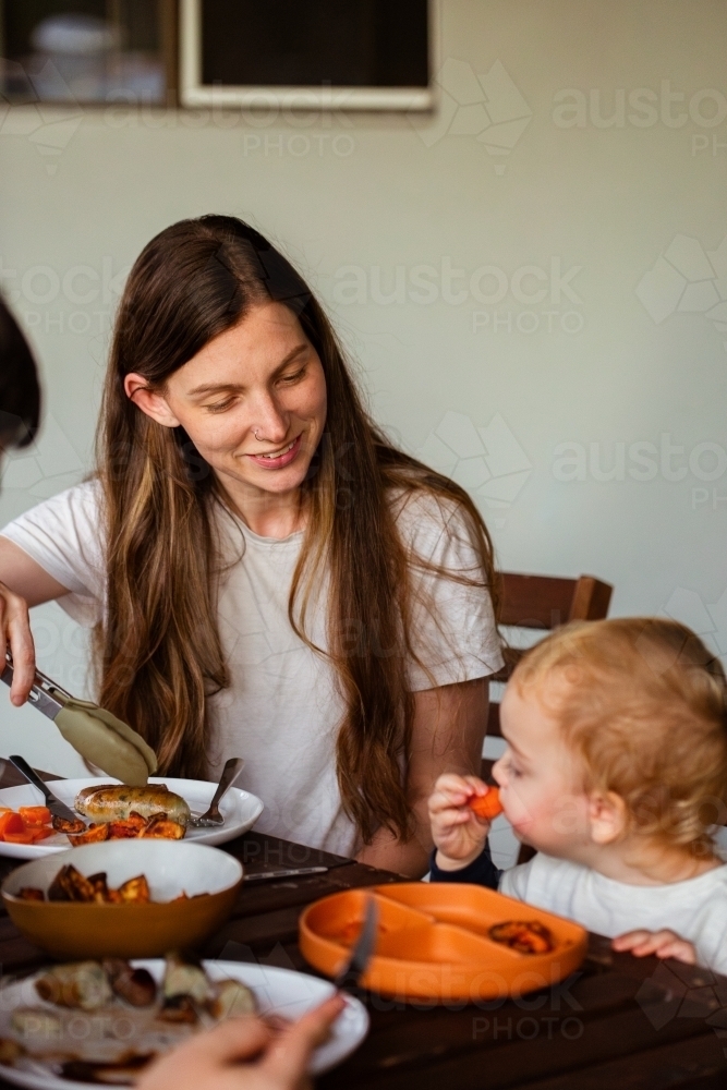 Image of mum serving up her dinner wile toddler eats at family BBQ in backyard at home ...