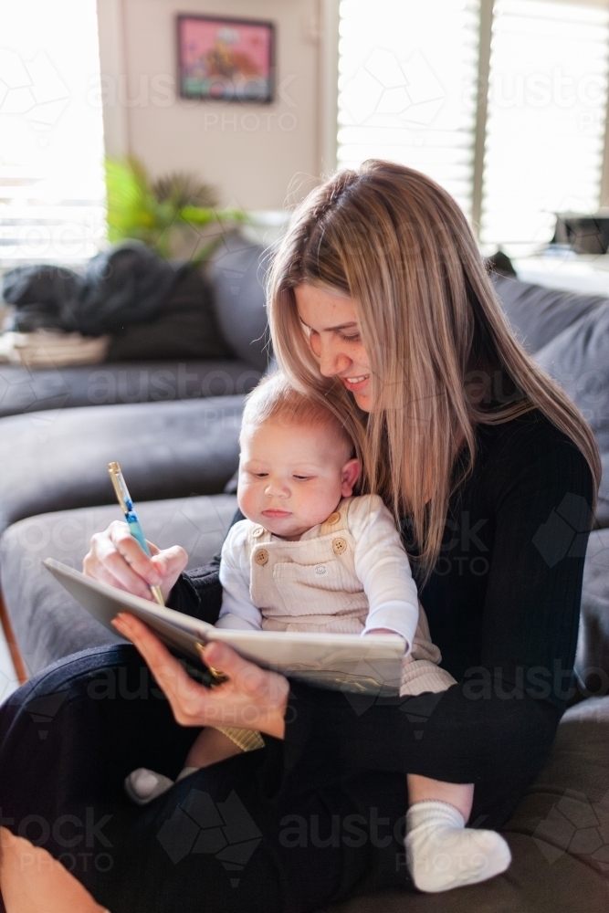 Image of Mum working from home with baby writing in journal planner ...