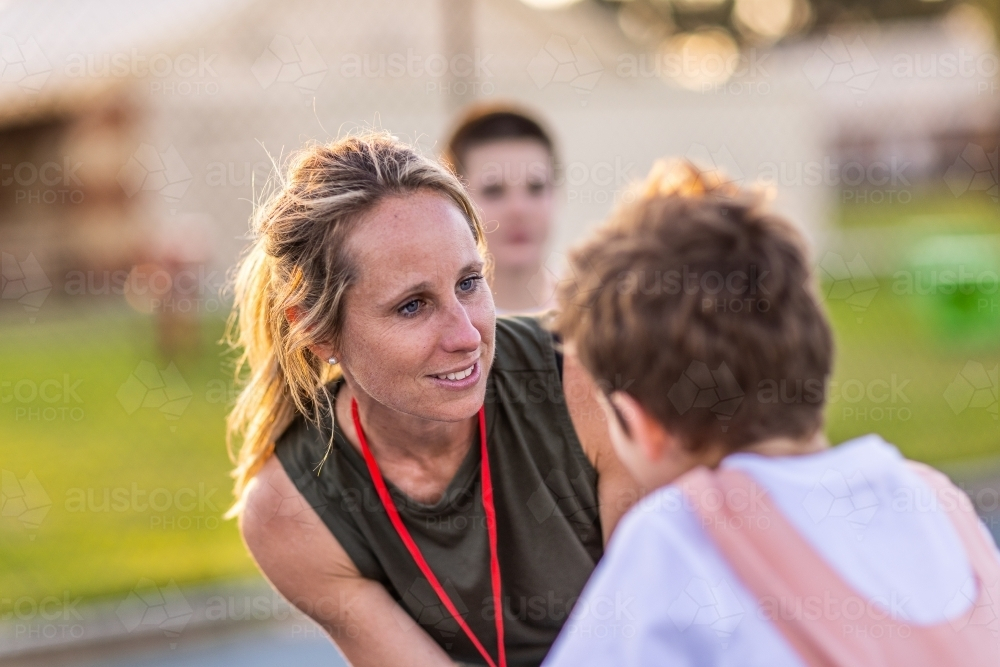 Image of netball coach bending to talk to young player - Austockphoto