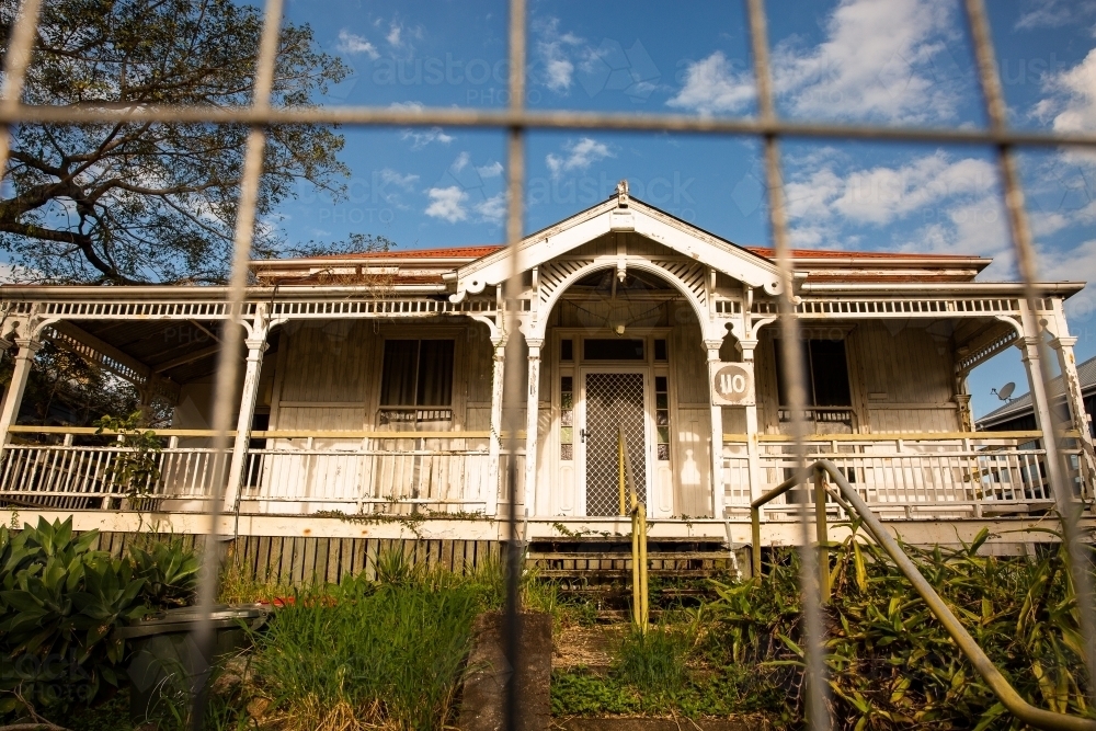 Image of old rundown queenslander behind a safety fence on a sunny day ...