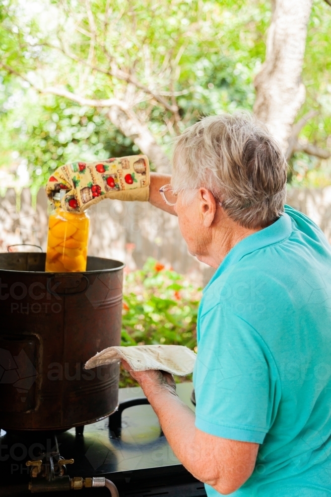 Image of Old woman canning fresh apricots - Austockphoto