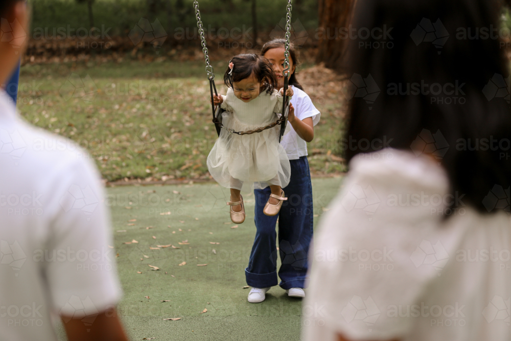 Image of Older sister pushing toddler girl on the swing at park ...