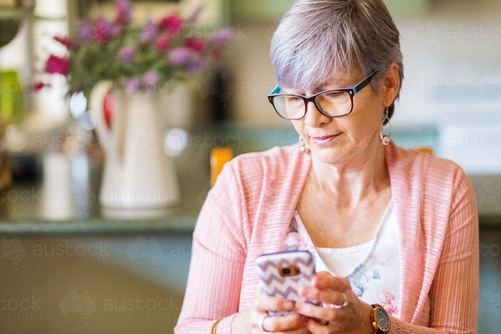 Image of Older woman texting on mobile phone inside home - Austockphoto