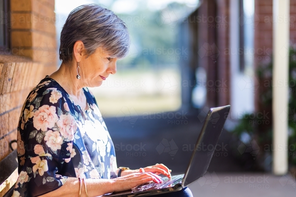 Image of Older woman typing on laptop sitting outside - Austockphoto