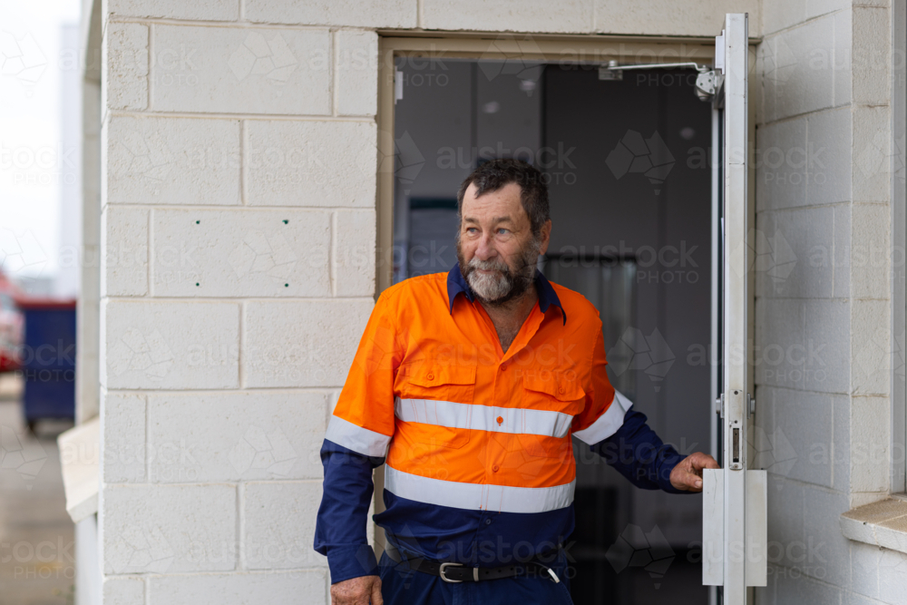 Image of Older working class man coming out of the offices glass door ...