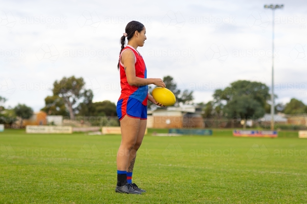 Image of one female aussie rules footballer standing on green grass ...