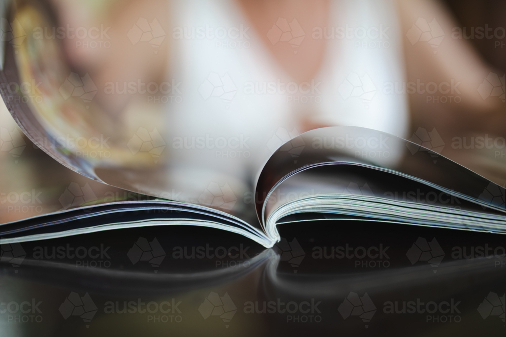Image of Open magazine on coffee table with out of focus woman in ...