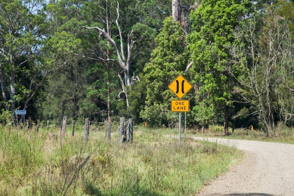 Image of Orange road narrows one lane sign beside unsealed rural road ...