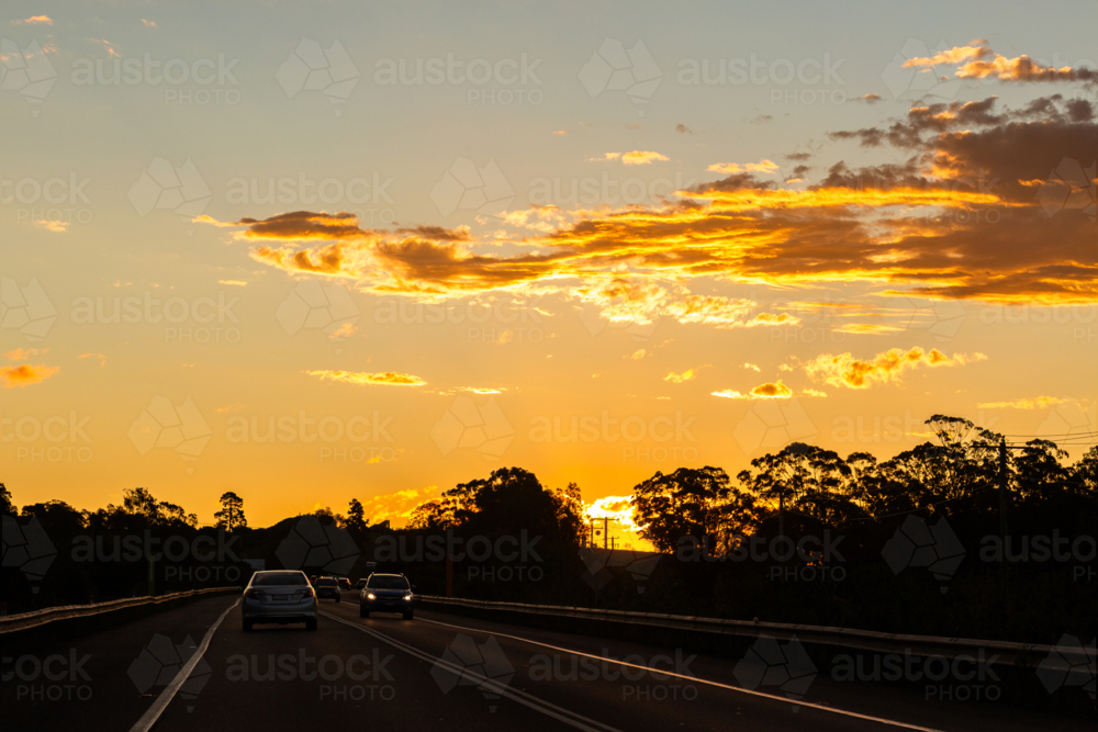 Image of Orange sunset sky over road with cars traveling on highway at ...