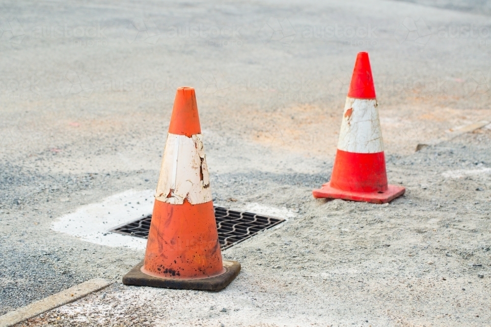 Image of Orange traffic cones and drain hole on road surface - Austockphoto