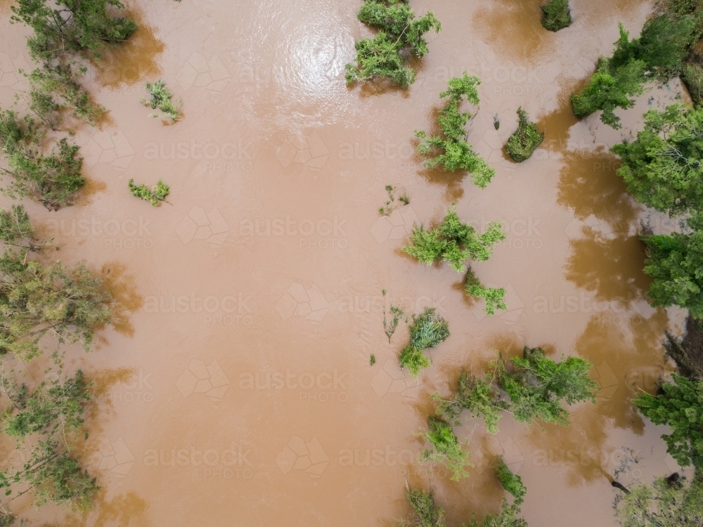 Image of Overhead view of rushing brown floodwaters overflowing river bank - Austockphoto