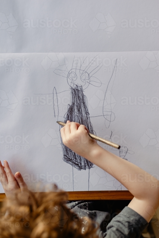 Image of Overhead view of child's drawing a figure with a pencil ...