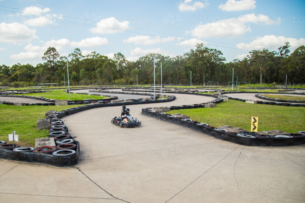 Image of People driving go karts around outdoor track - Austockphoto
