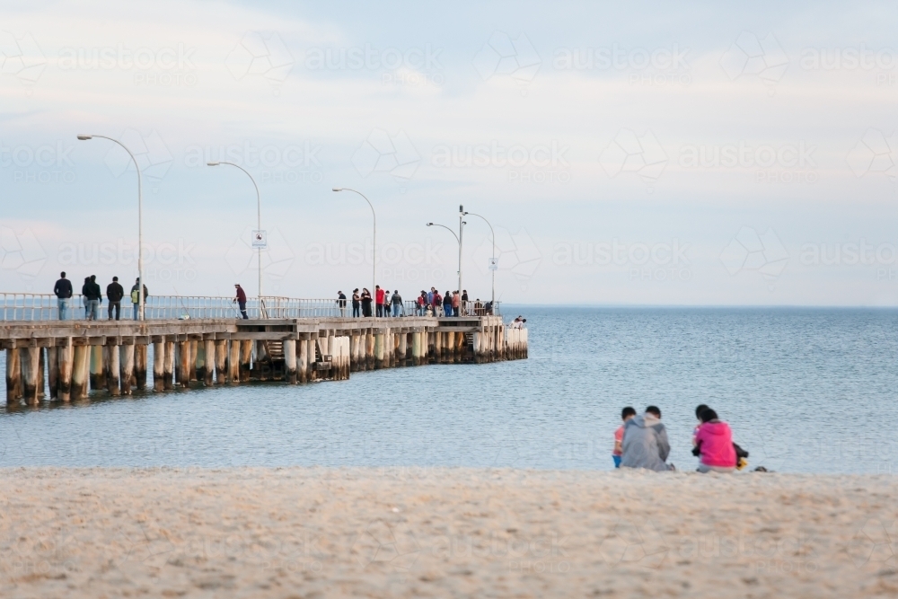 Image of People on the beach and walking on a pier at dusk - Austockphoto