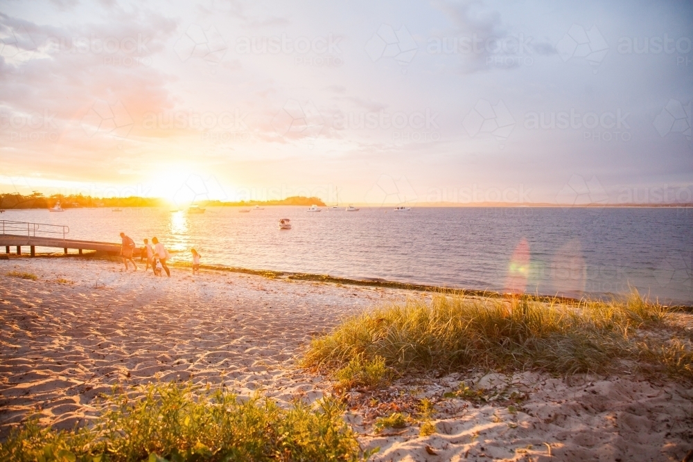 Image of People walking across a beach at sunset over the headland ...