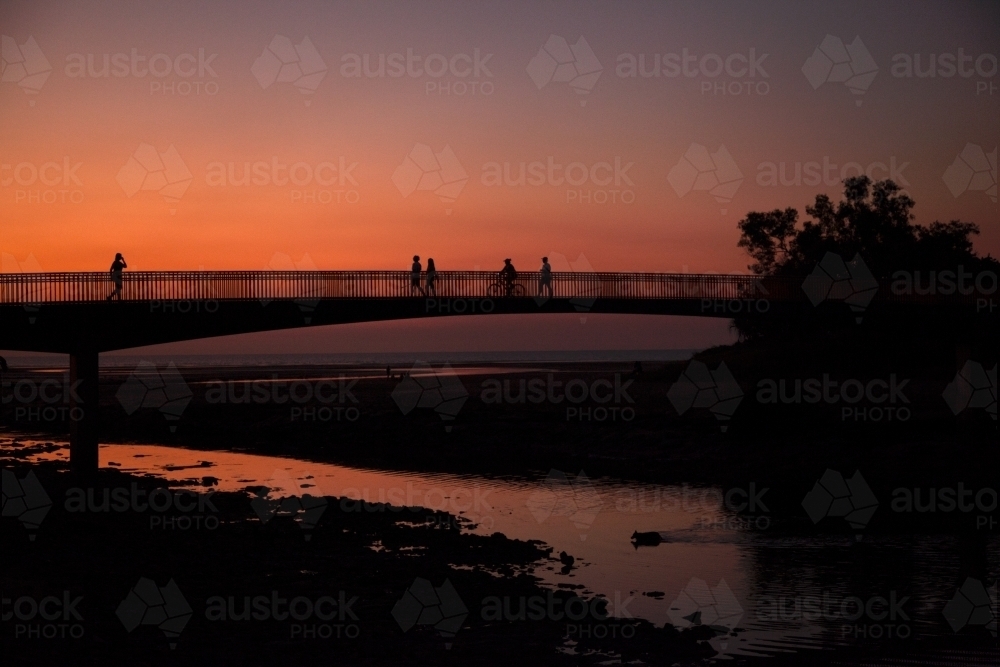 Image of People walking across bridge at sunset - Austockphoto
