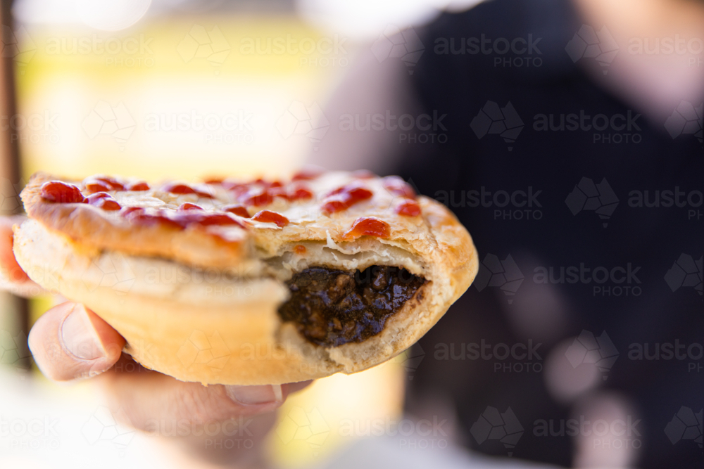 Image of person holding a meat pie with bite missing - Austockphoto