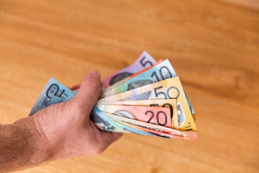Image of person holding a wad of Australian bank notes - Austockphoto