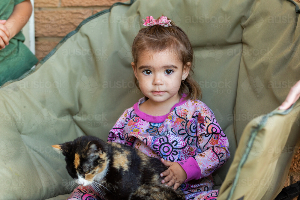 Image of Pet cat sitting on toddler girls lap in chair outside home ...