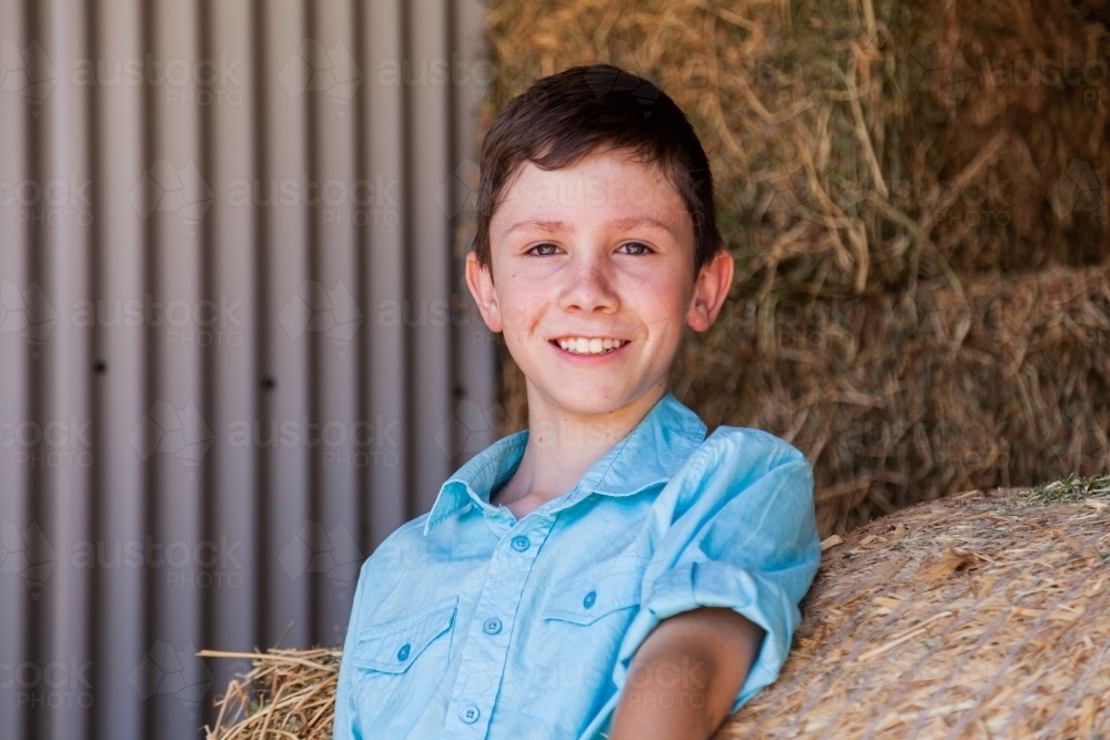 Image of Portrait of a happy young boy on hay bales in a shed ...