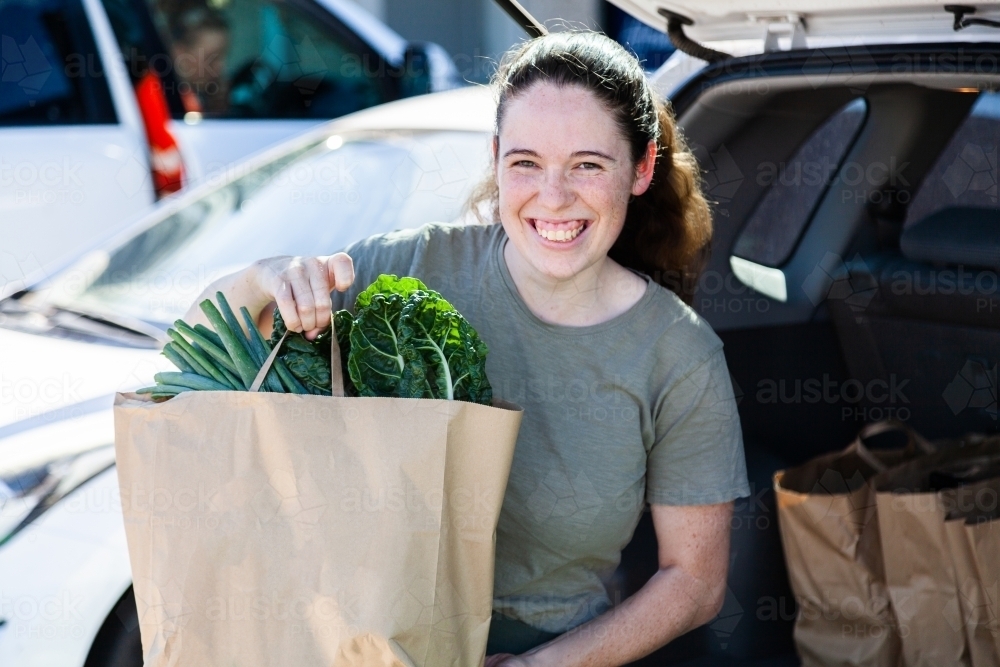 Image of Portrait of a happy young woman loading groceries into the car ...