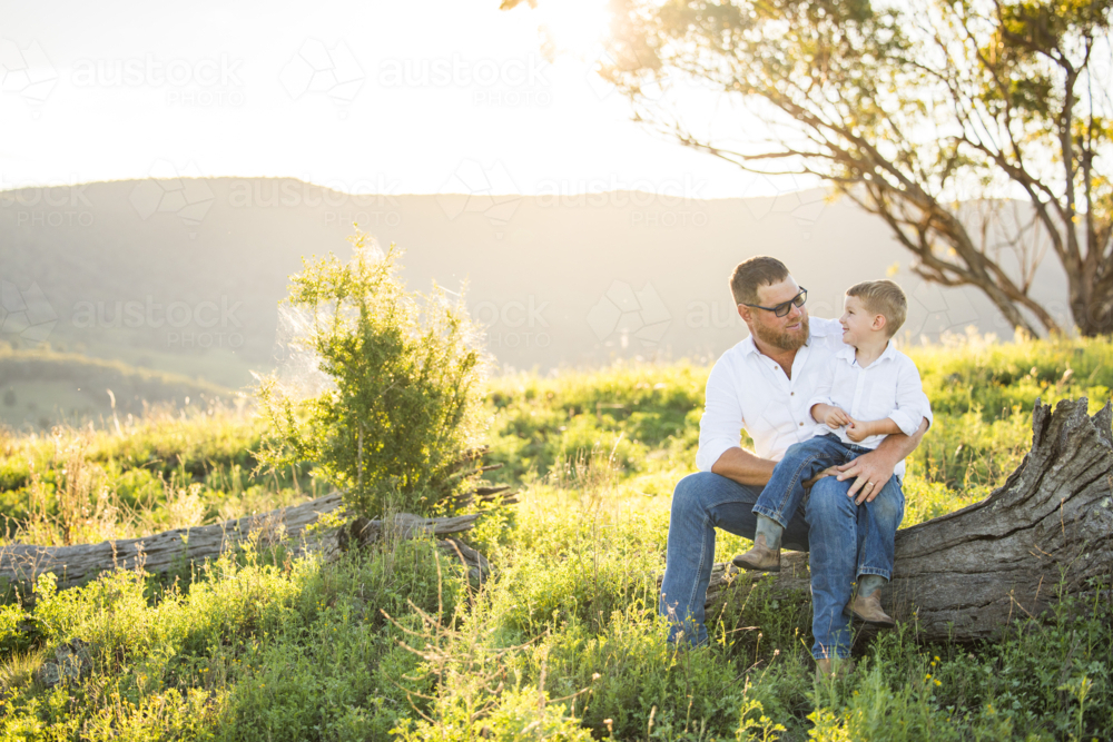 Image of Portrait of father and son sitting together on log on ...
