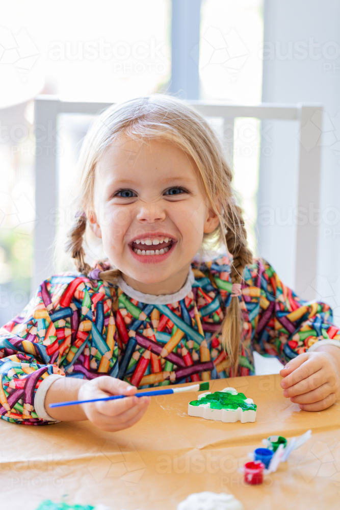 Image of Portrait of grinning little girl in art smock painting ...
