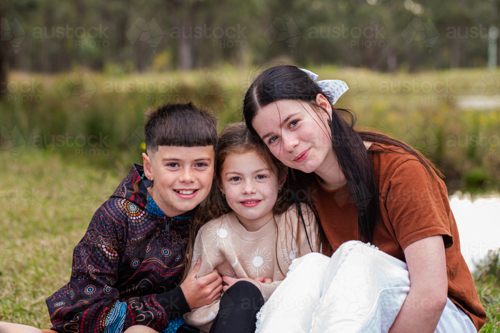 Image of Portrait of three siblings sitting together outside - Austockphoto