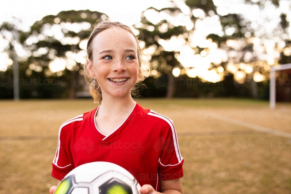Image of Portrait of tween girl in a red uniform holding a football and ...