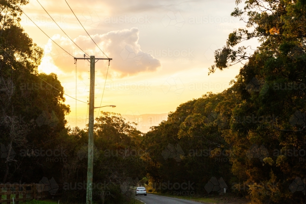 Image of power poles beside narrow road at sunset with car traveling ...