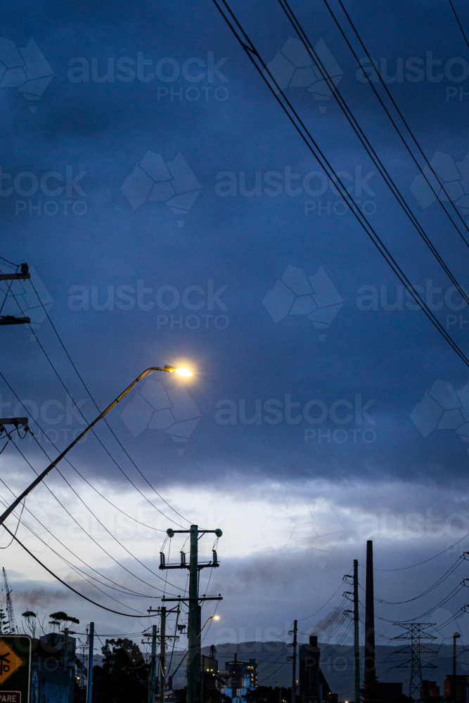 Image of Powerlines and street light against dark clouds in sky ...