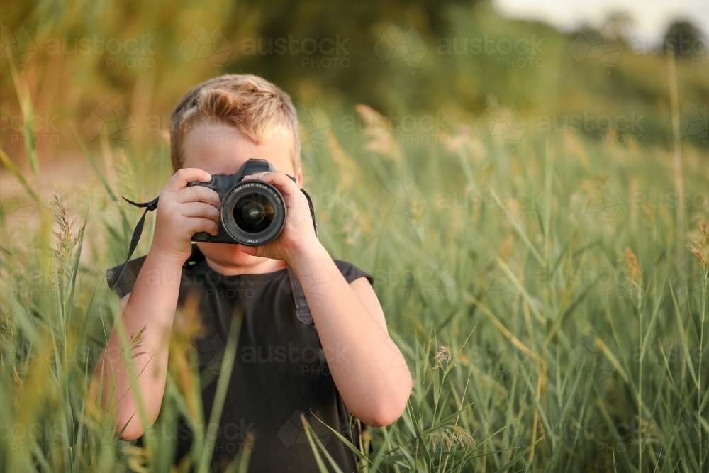 Image of Pre-teen boy in long grass taking photos with DSLR camera ...