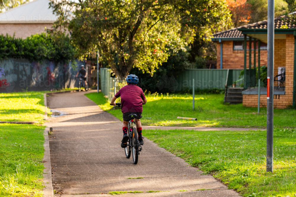Image of Preteen boy riding away down footpath behind houses - Austockphoto