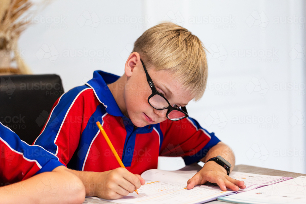 Image of Primary aged boy working on homework workbook after school ...