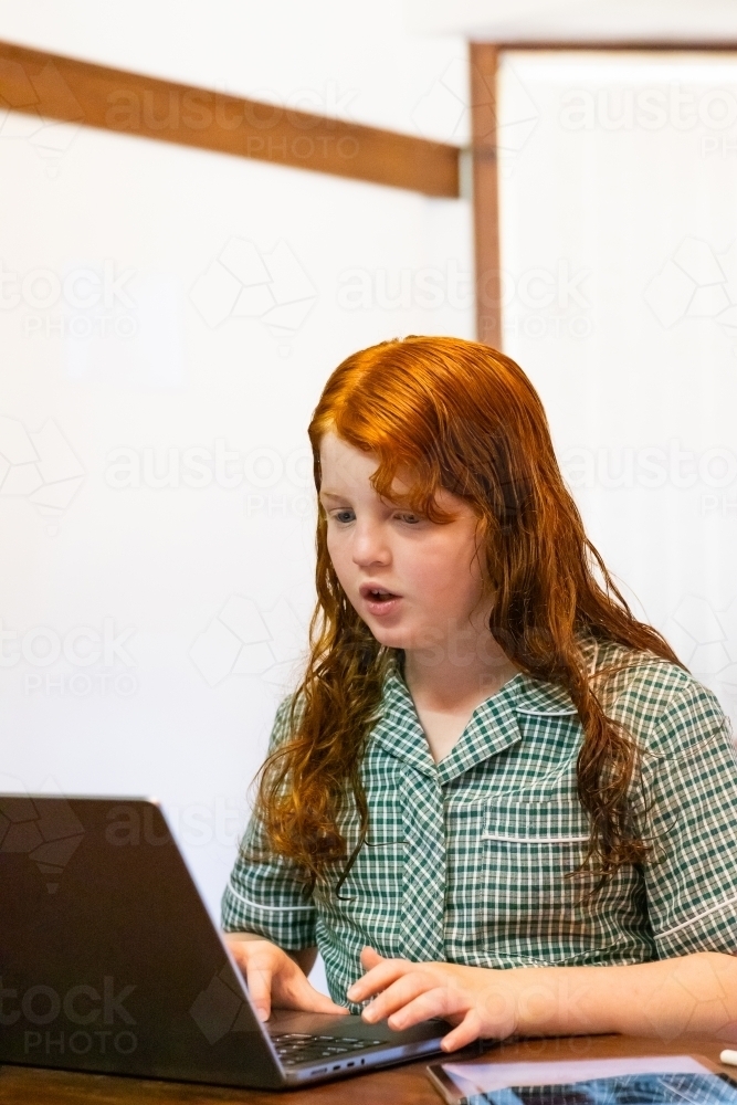 Image of primary school student in school uniform doing work on laptop ...