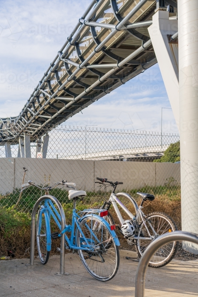 Image of Push bikes parked under an elevated modern metal footbridge ...