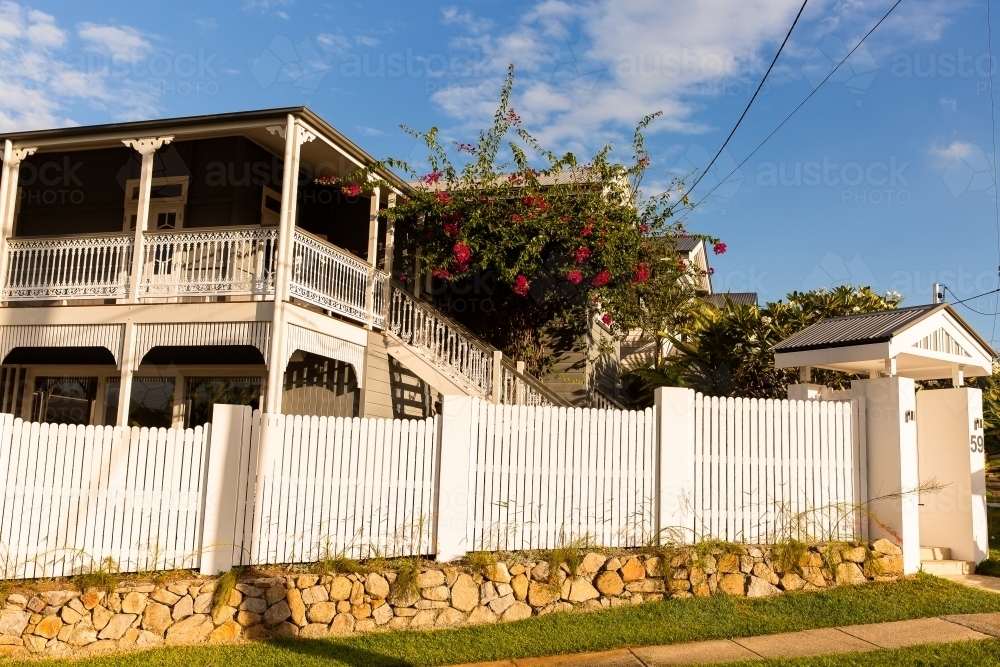 Image of queenslander house with a white front fence in the afternoon ...