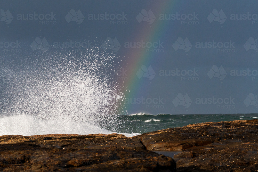 Image of Rainbow behind crashing wave and coastal rock shelf ...