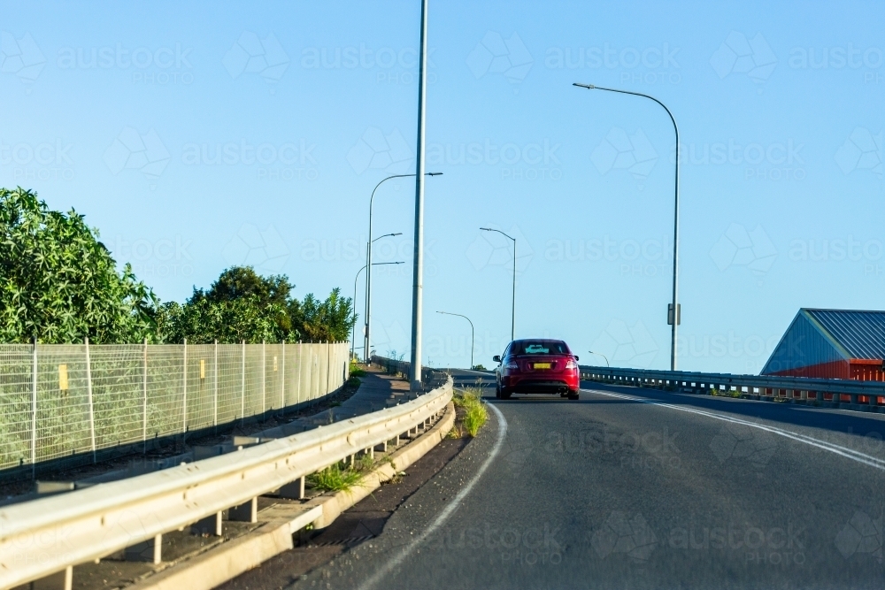 Image of Red car driving over bridge out of town traveling on road ...