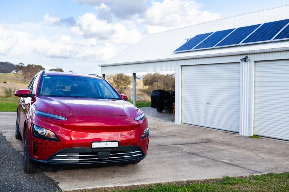Image of Red electric car beside shed garage with solar panels on roof ...