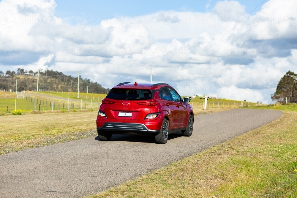 Image of Red electric vehicle car driving down narrow country road on ...