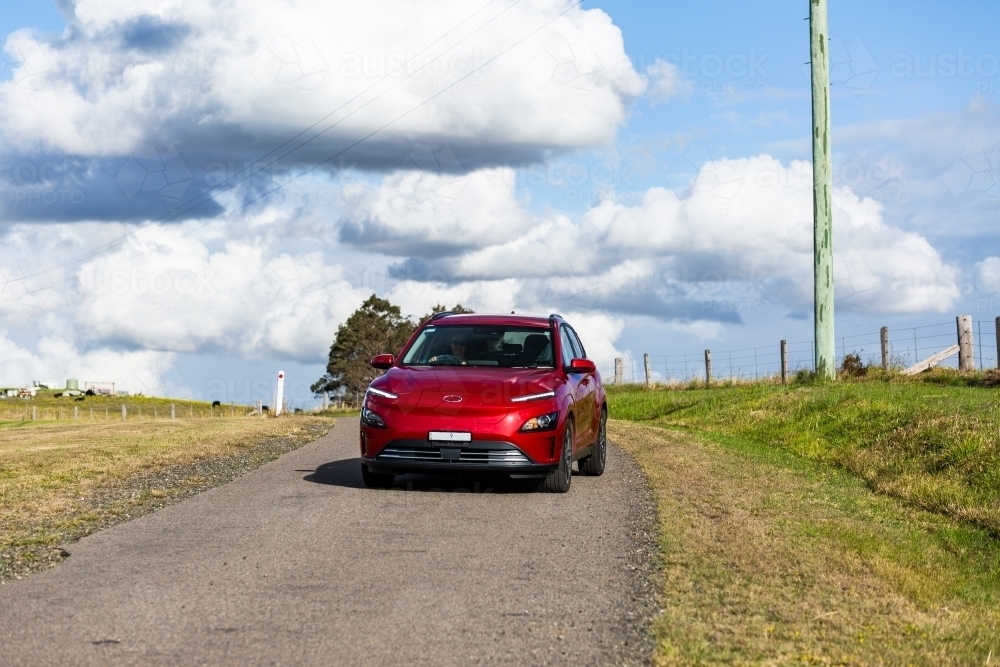 Image of Red electric vehicle car driving down rural country road on ...