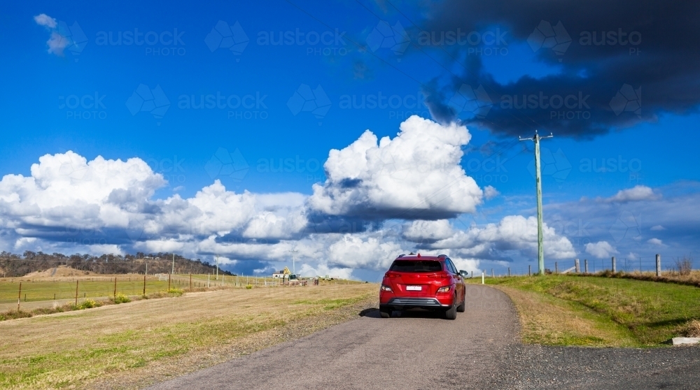 Image of Red electric vehicle car driving down rural country road on ...