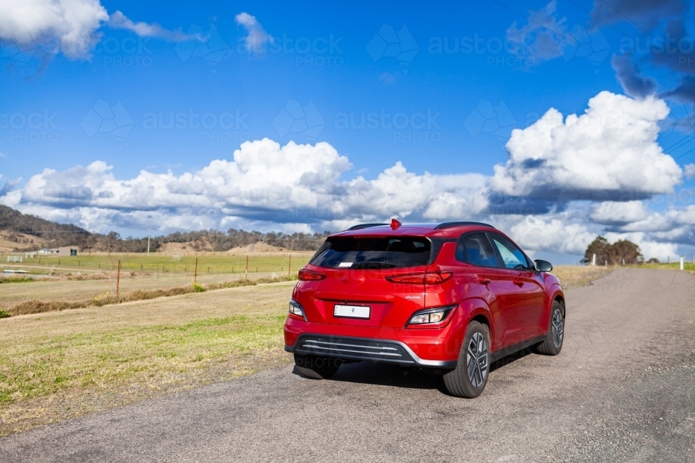 Image of Red electric vehicle car driving down rural country road on ...