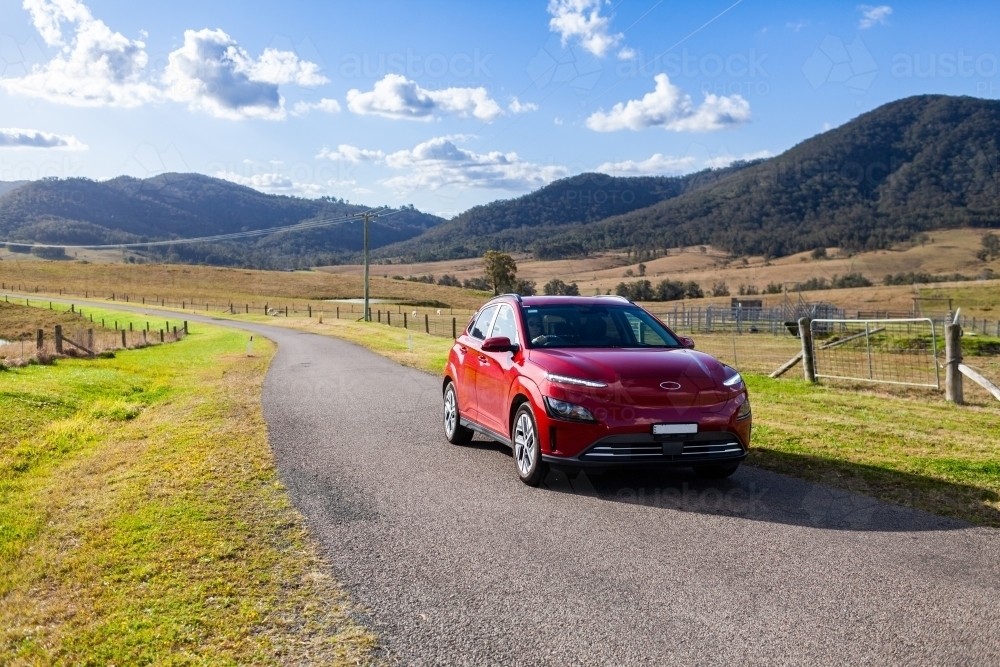 Image of Red electric vehicle car driving down rural country road on ...
