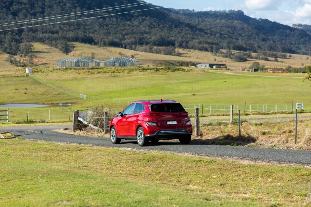 Image of Red electric vehicle car driving down rural country road on ...