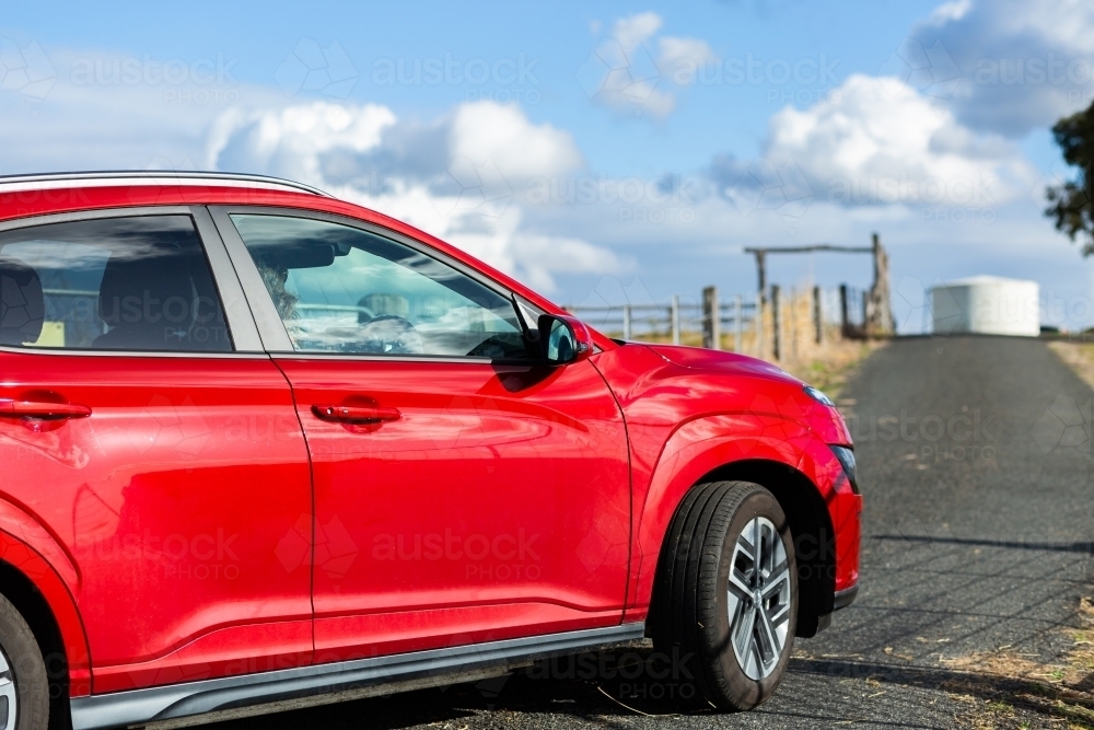 Image of Red ev car driving into driveway of rural property - Austockphoto